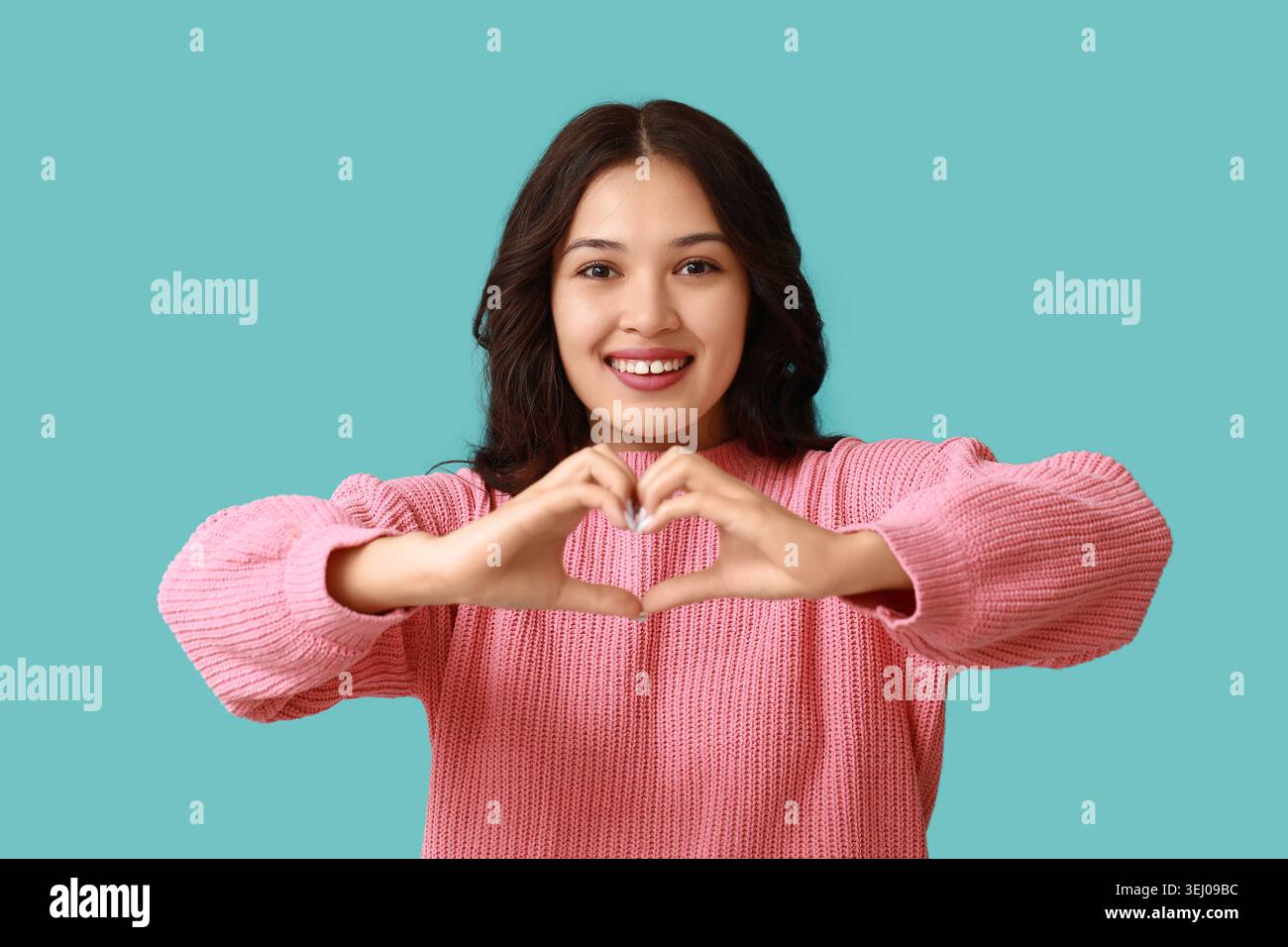 Pretty young Asian woman showing heart gesture on blue background ...
