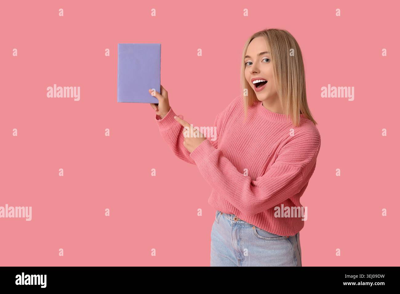 Beautiful young woman pointing at book on pink background Stock Photo ...