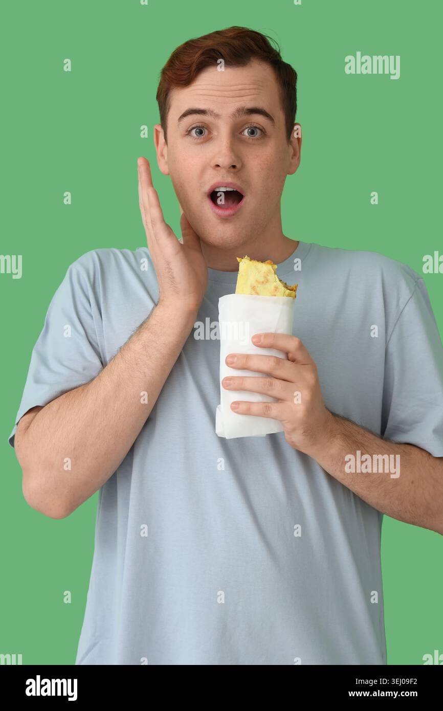 Surprised young man with tasty sandwich wrap on green background Stock ...