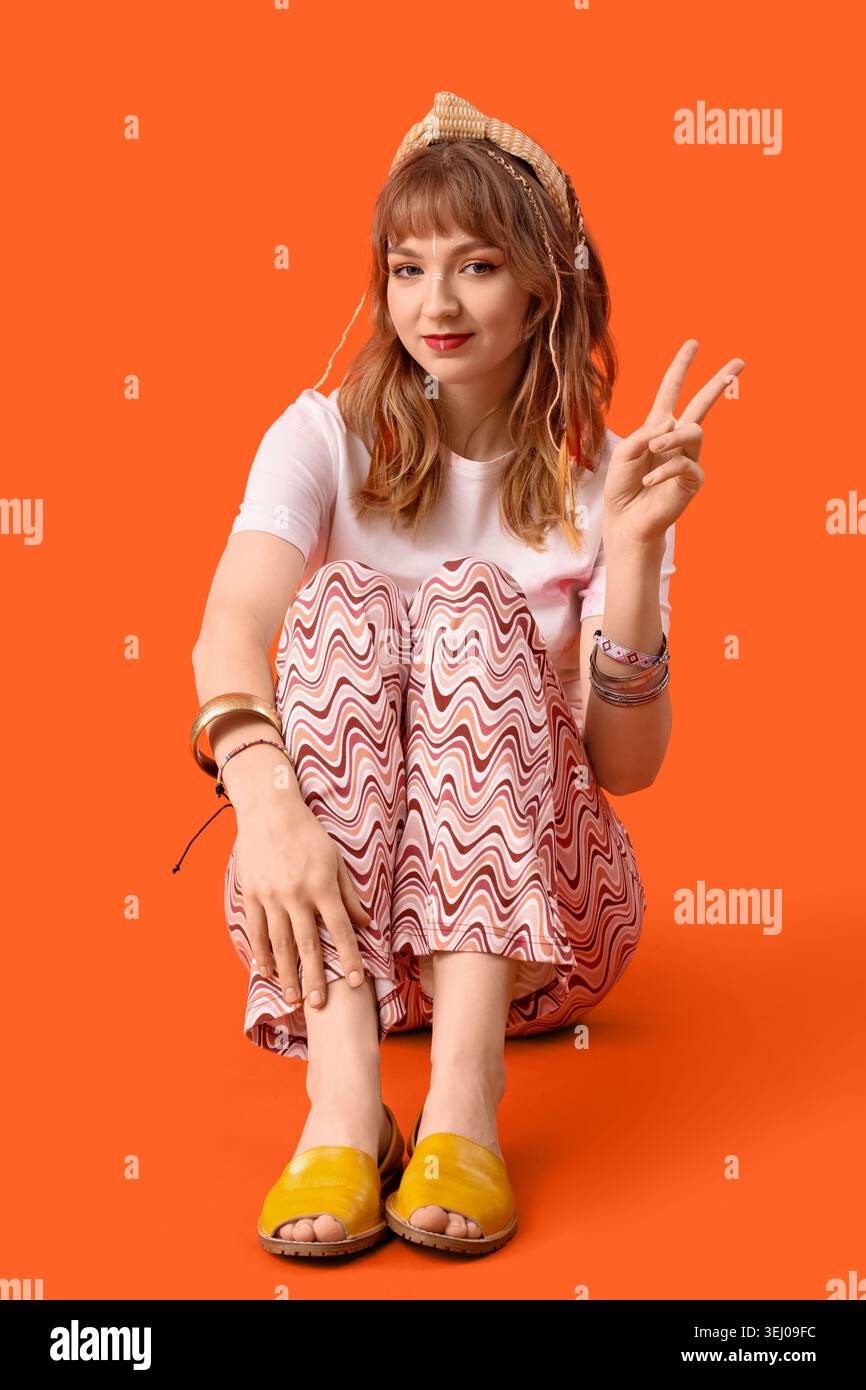 Female hippie showing victory gesture on orange background Stock Photo ...
