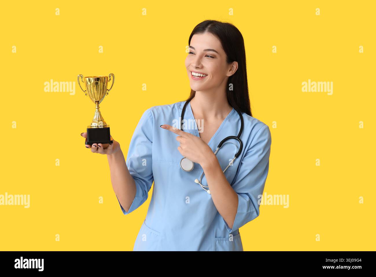 Female doctor pointing at gold cup on yellow background Stock Photo - Alamy