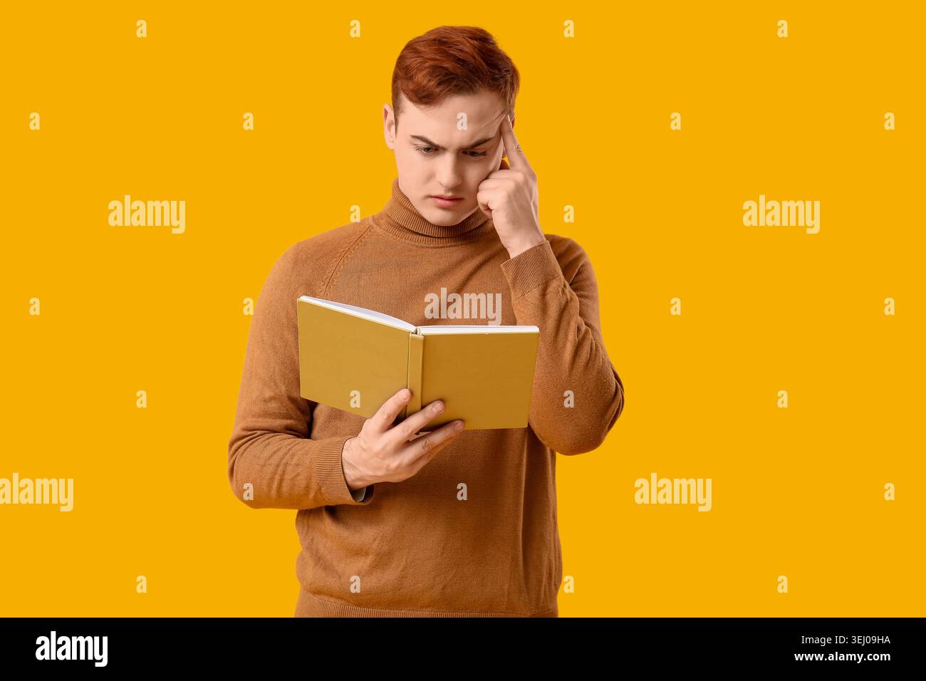 Thoughtful young man reading book on yellow background Stock Photo - Alamy