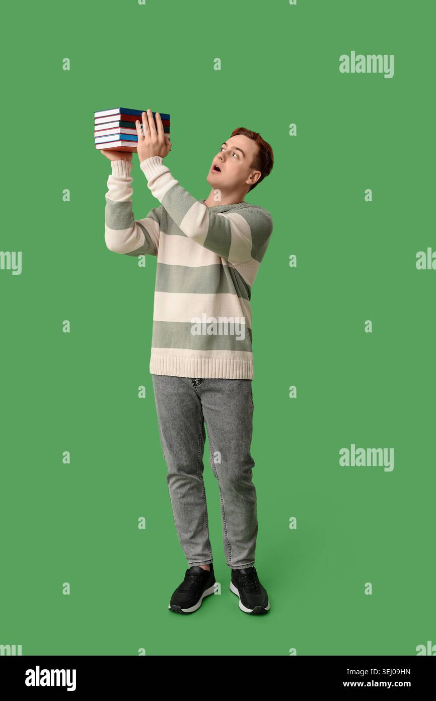 Emotional man holding stack of books on green background Stock Photo ...