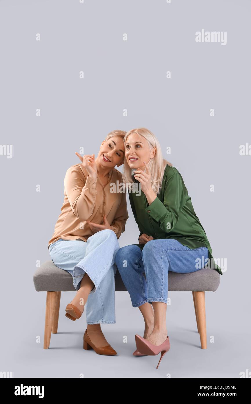 Beautiful mature women sitting on bench against grey background Stock ...