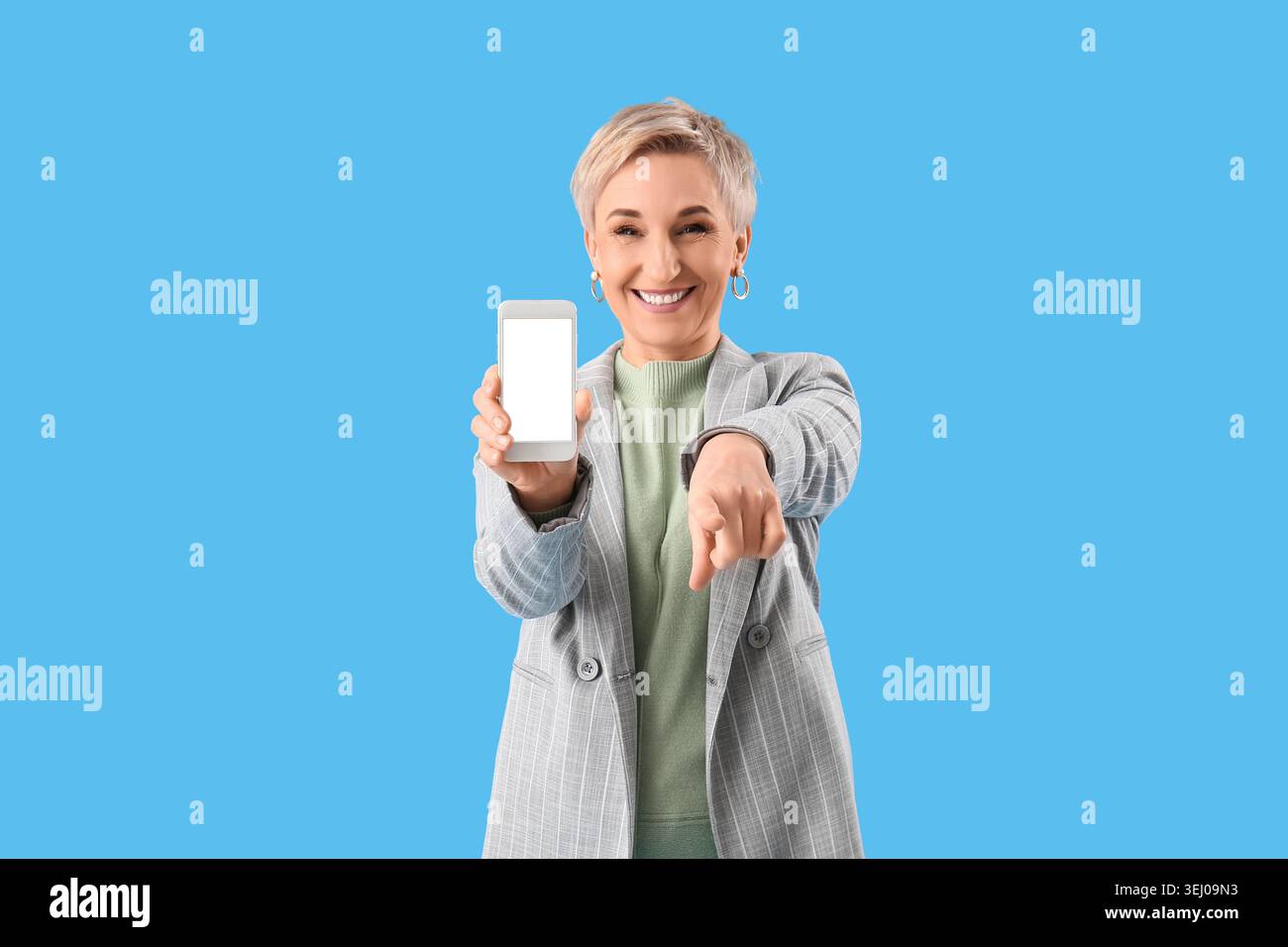 Happy mature woman with smartphone pointing at viewer on light blue ...