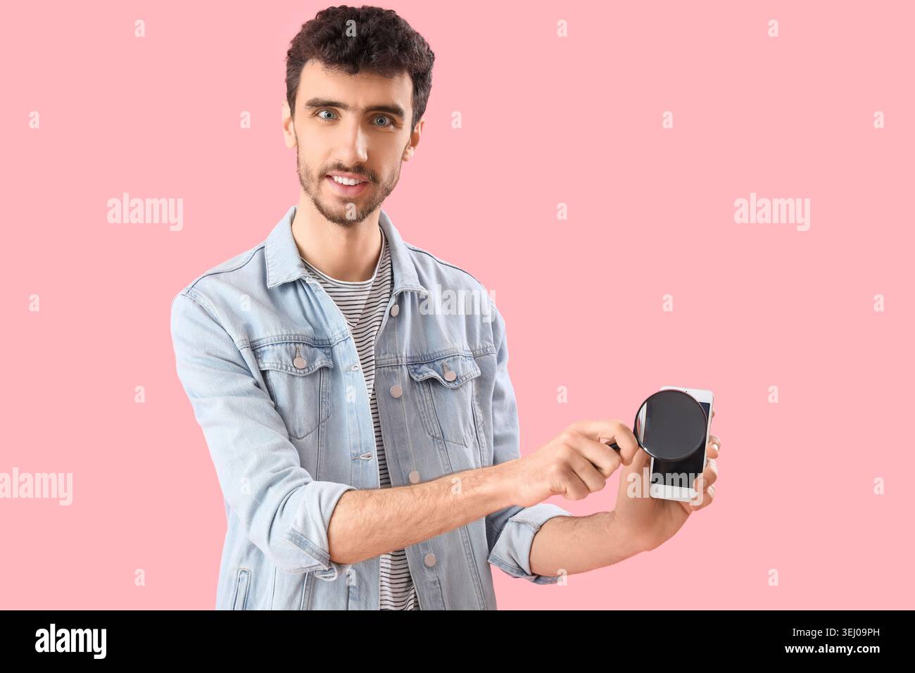 Handsome young man with magnifier and mobile phone on pink background ...