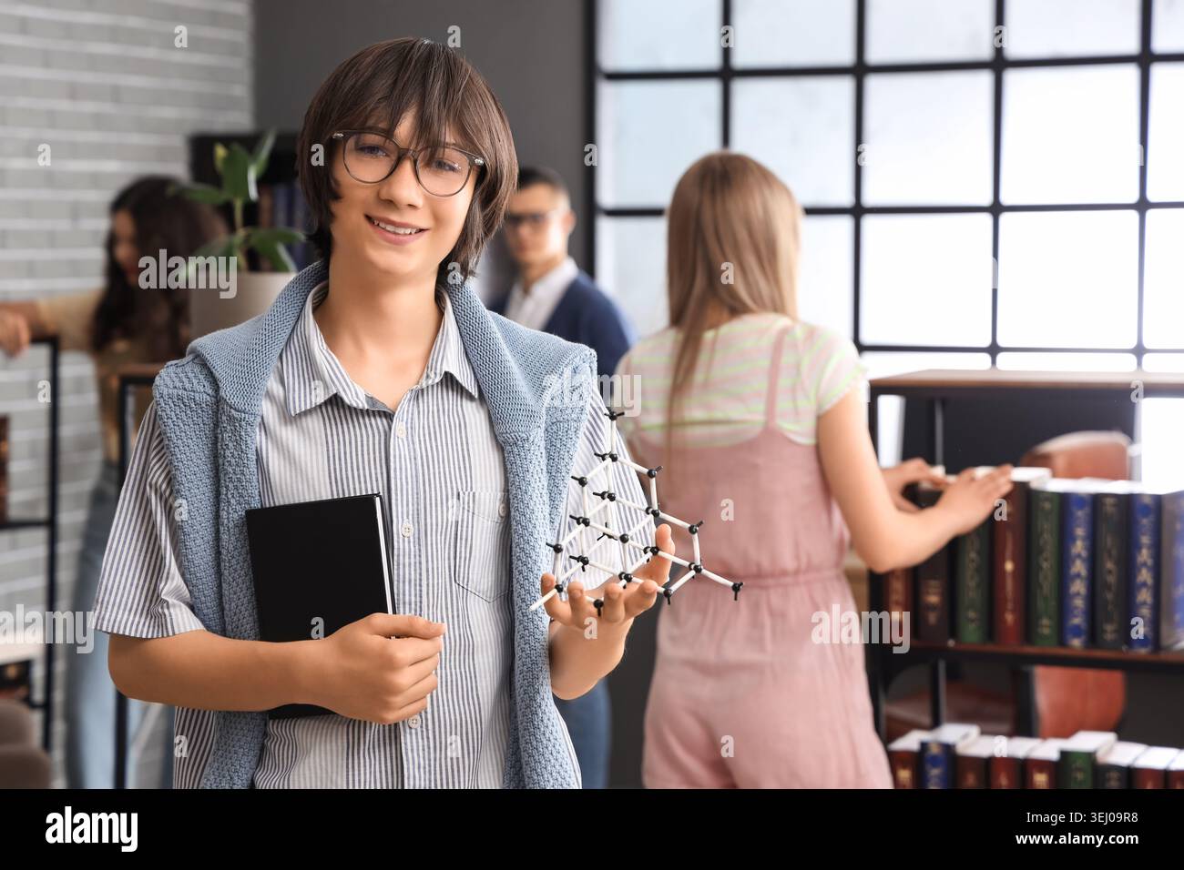 Male student with book and molecular model in library Stock Photo - Alamy