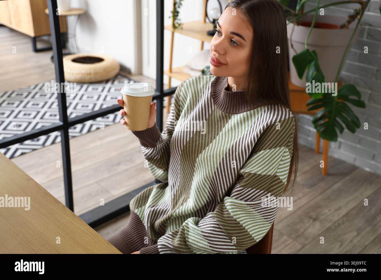 Young woman with cup of coffee sitting at table in office Stock Photo ...