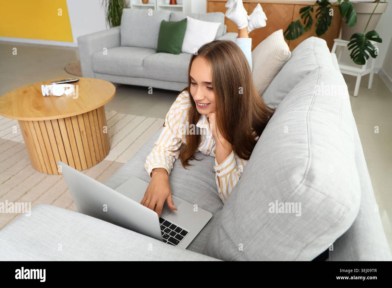 Young woman using laptop on couch in living room Stock Photo - Alamy