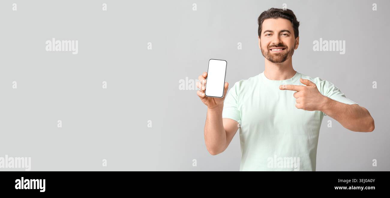 Young man pointing at modern mobile phone on grey background with space ...