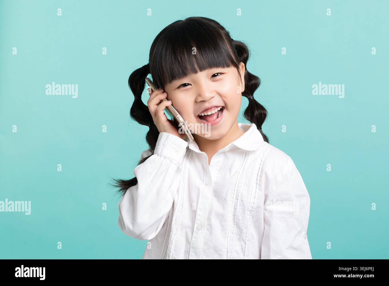 An Asian girl happily uses a smartphone against a blue background ...