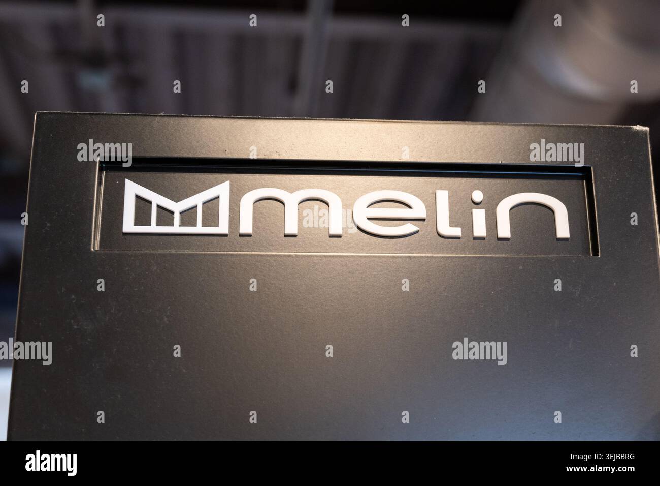 Close-up of Melin logo sign on dark display inside retail space ...