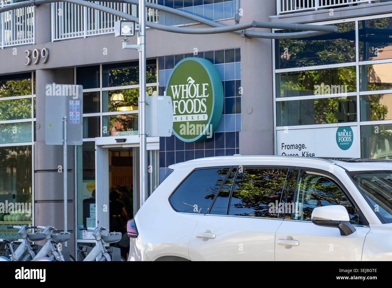Whole Foods Market entrance with logo on urban building and parked car ...