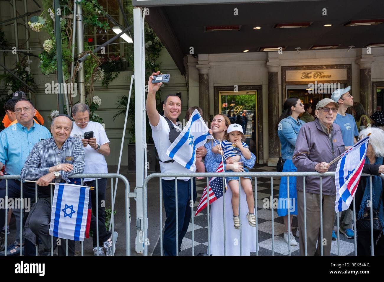 People stand behind a metal barrier, holding Israeli and American flags ...
