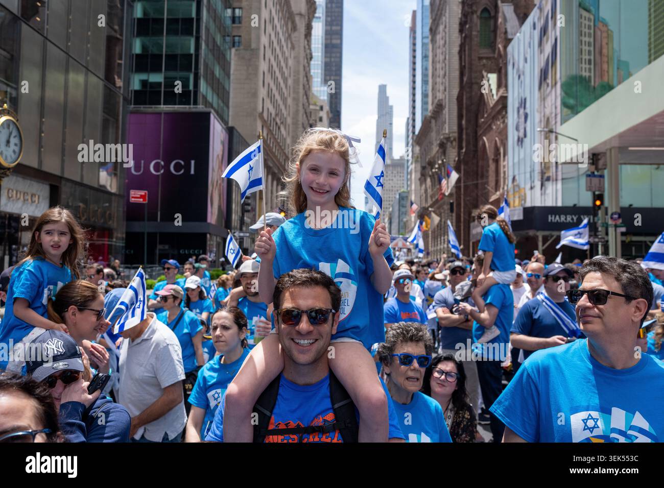 A diverse crowd walks down a city street, many holding Israeli flags ...