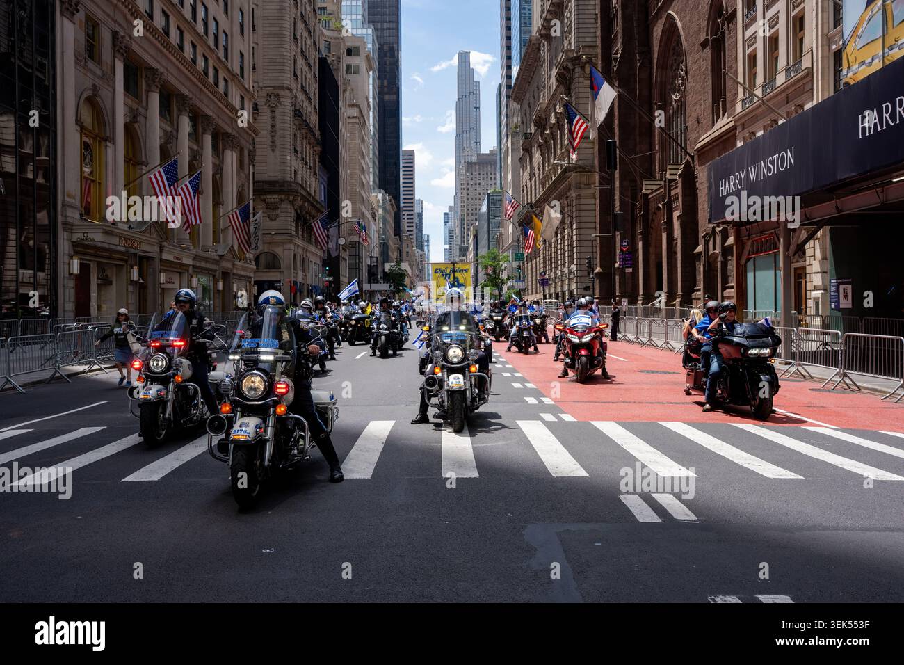 A police motorcycle procession rides down a city street lined with tall ...