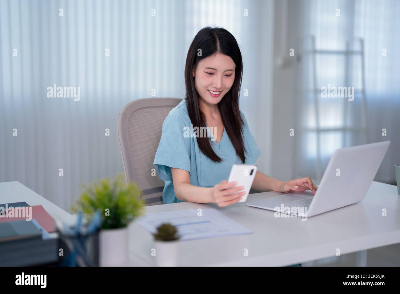 Asian woman using laptop and smartphone while working at modern home ...