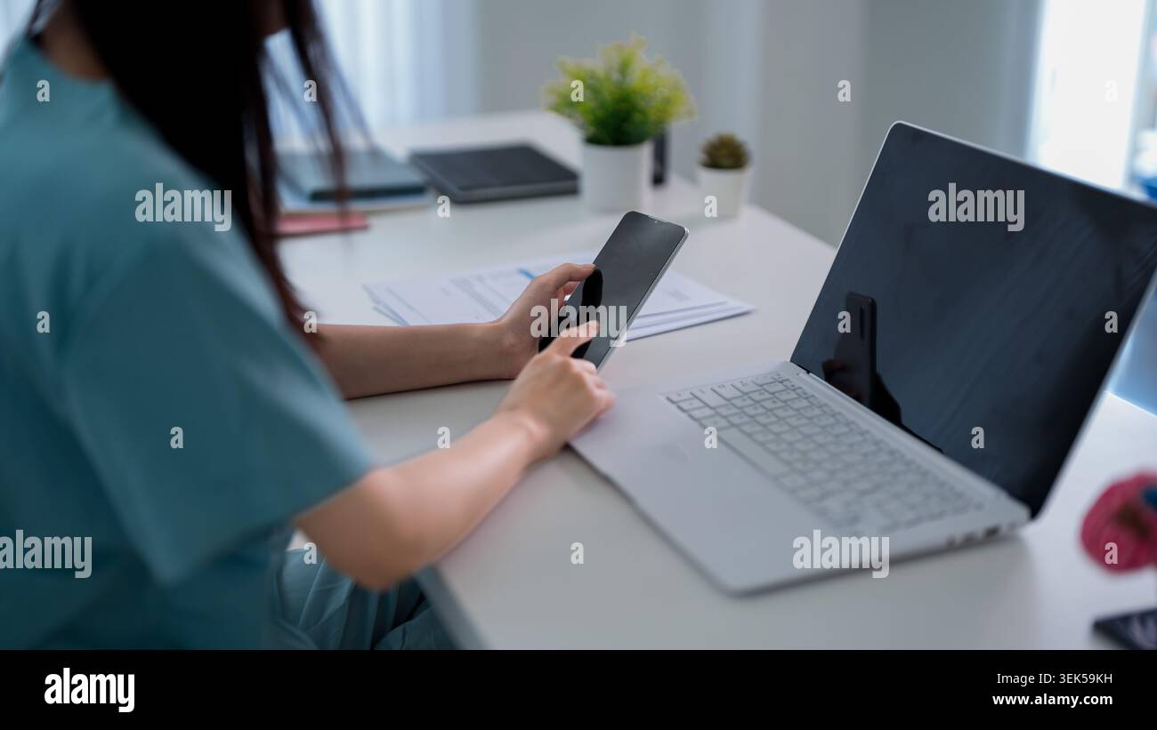 Asian woman using smartphone and laptop computer at home office desk ...