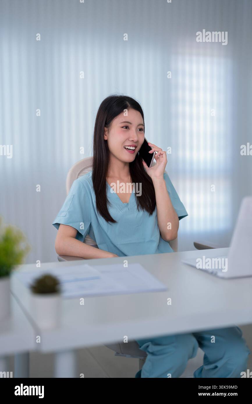 Young Asian woman doctor in blue scrubs talking on smartphone at modern ...