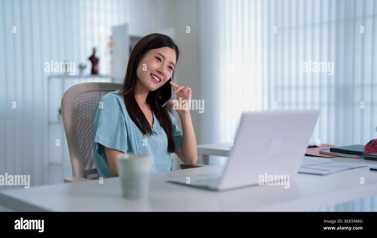 Asian medical professional sitting at desk using laptop while talking ...