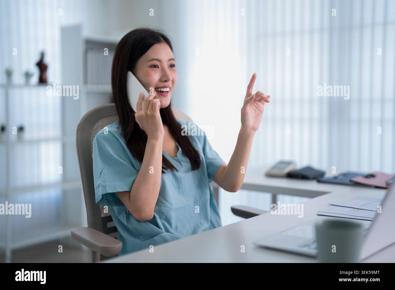 Happy Asian women doctor talking on mobile phone gesturing while ...