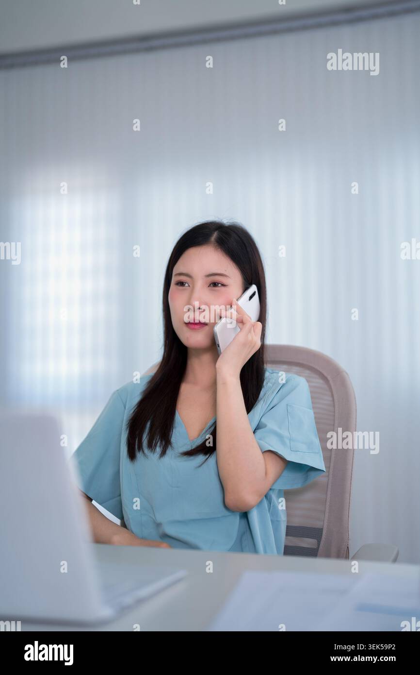 Asian female doctor talking on phone in hospital clinic office for ...