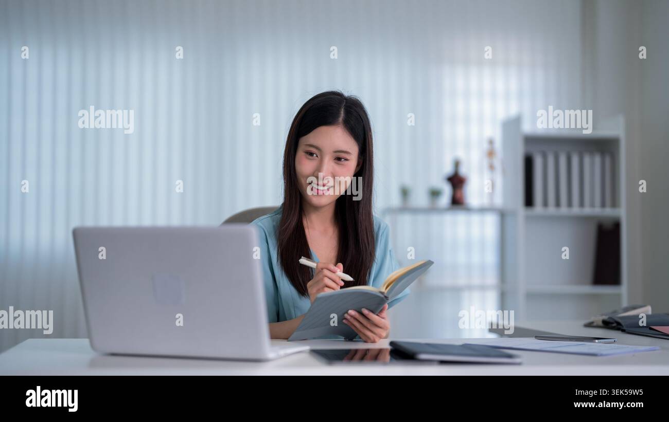 Young adult Asian woman professional writing notes in journal at desk ...