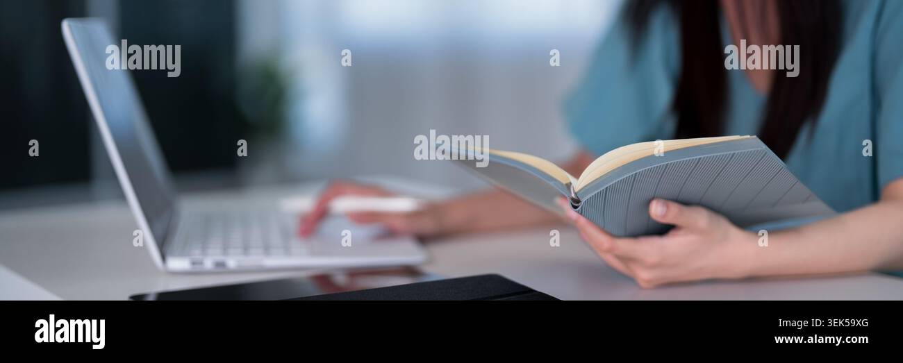 Asian women reading book at desk with laptop computer for professional ...