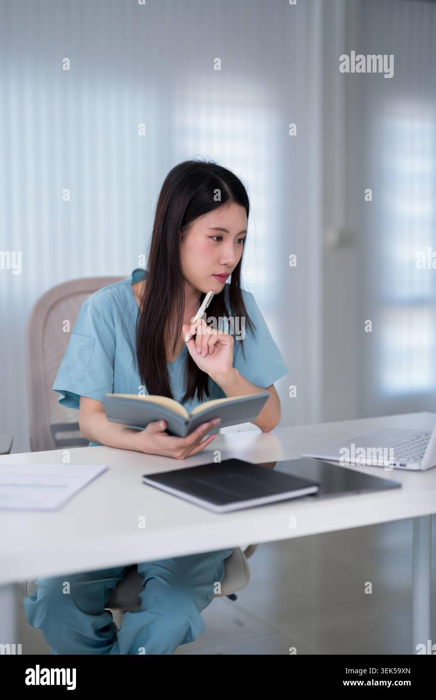 Young Asian female doctor healthcare worker studying from medical book ...