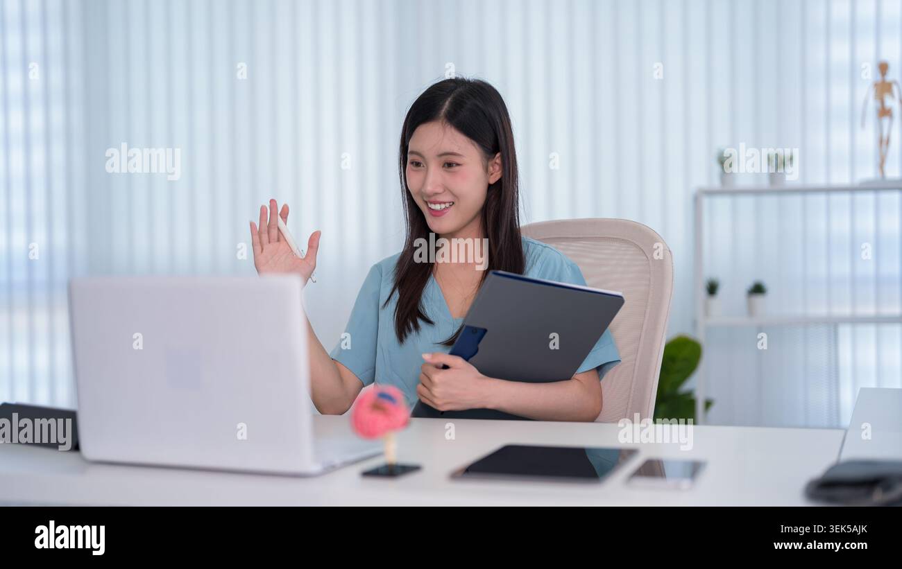 Young Asian professional medical worker waving during telehealth video ...