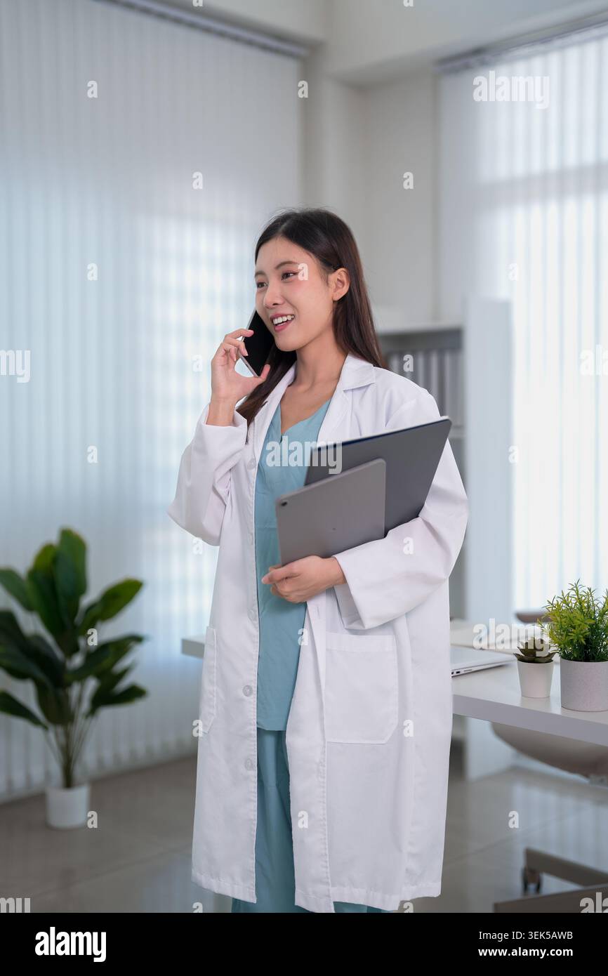 Young Asian woman doctor in white coat talking on smartphone while ...