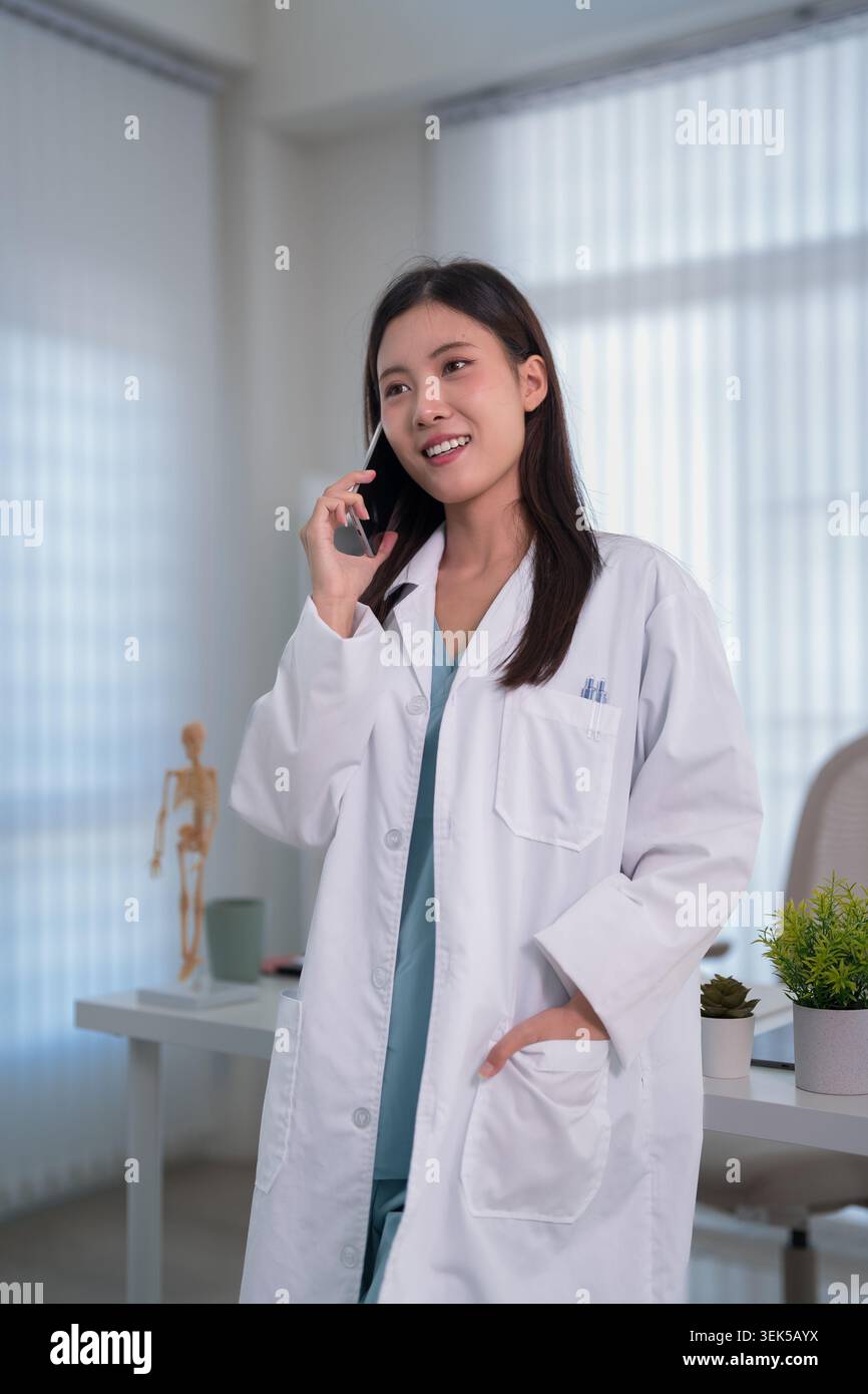 Asian female doctor in white coat talking on phone at modern clinic ...