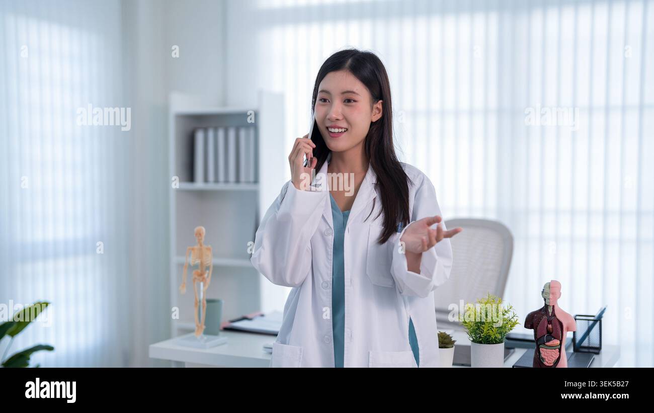 Asian female doctor in white coat talking on phone while gesturing in ...