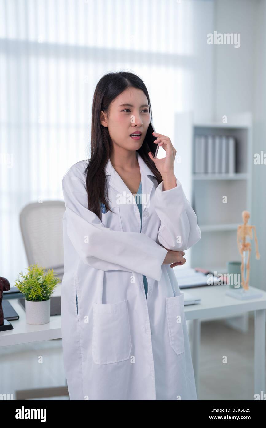 Asian female doctor talking on mobile phone in modern medical clinic ...