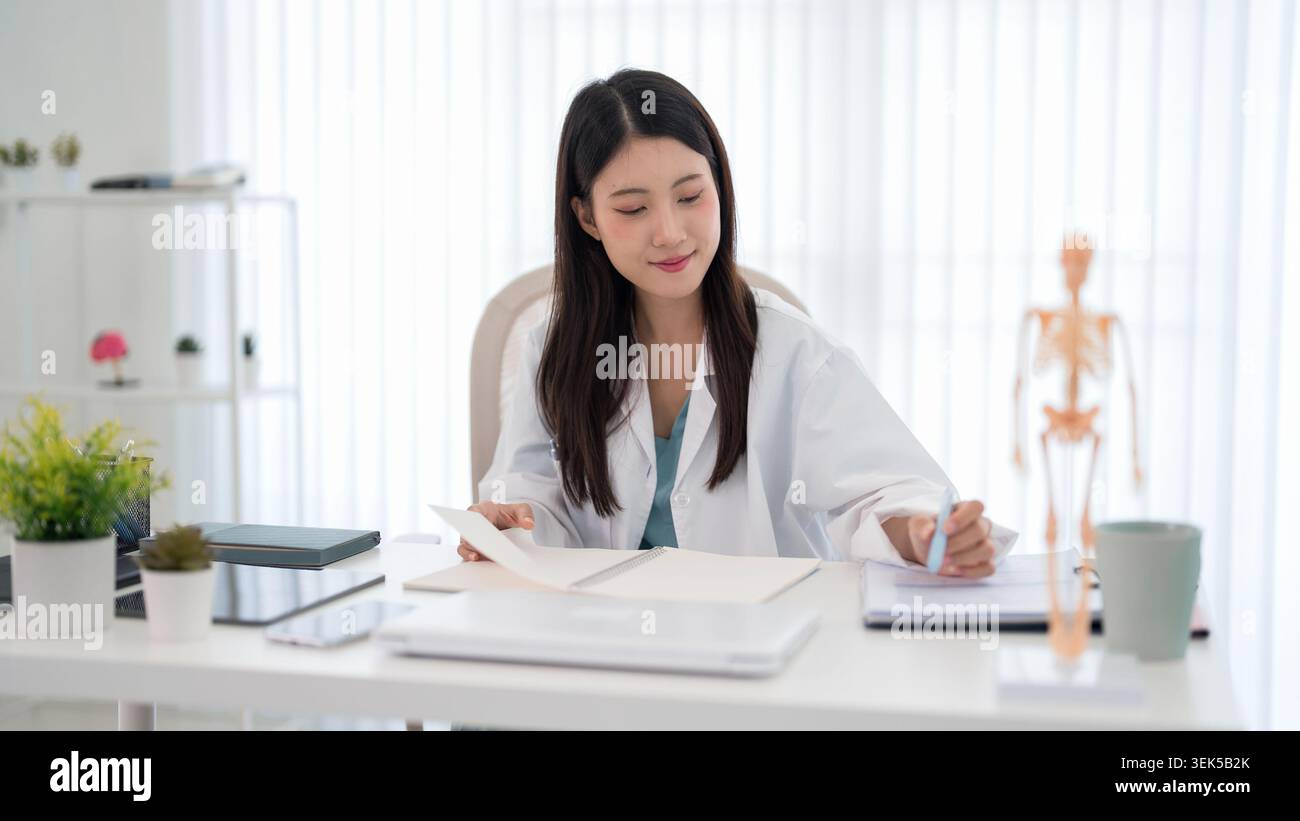 Young Asian woman doctor in white coat reviewing medical paperwork and ...