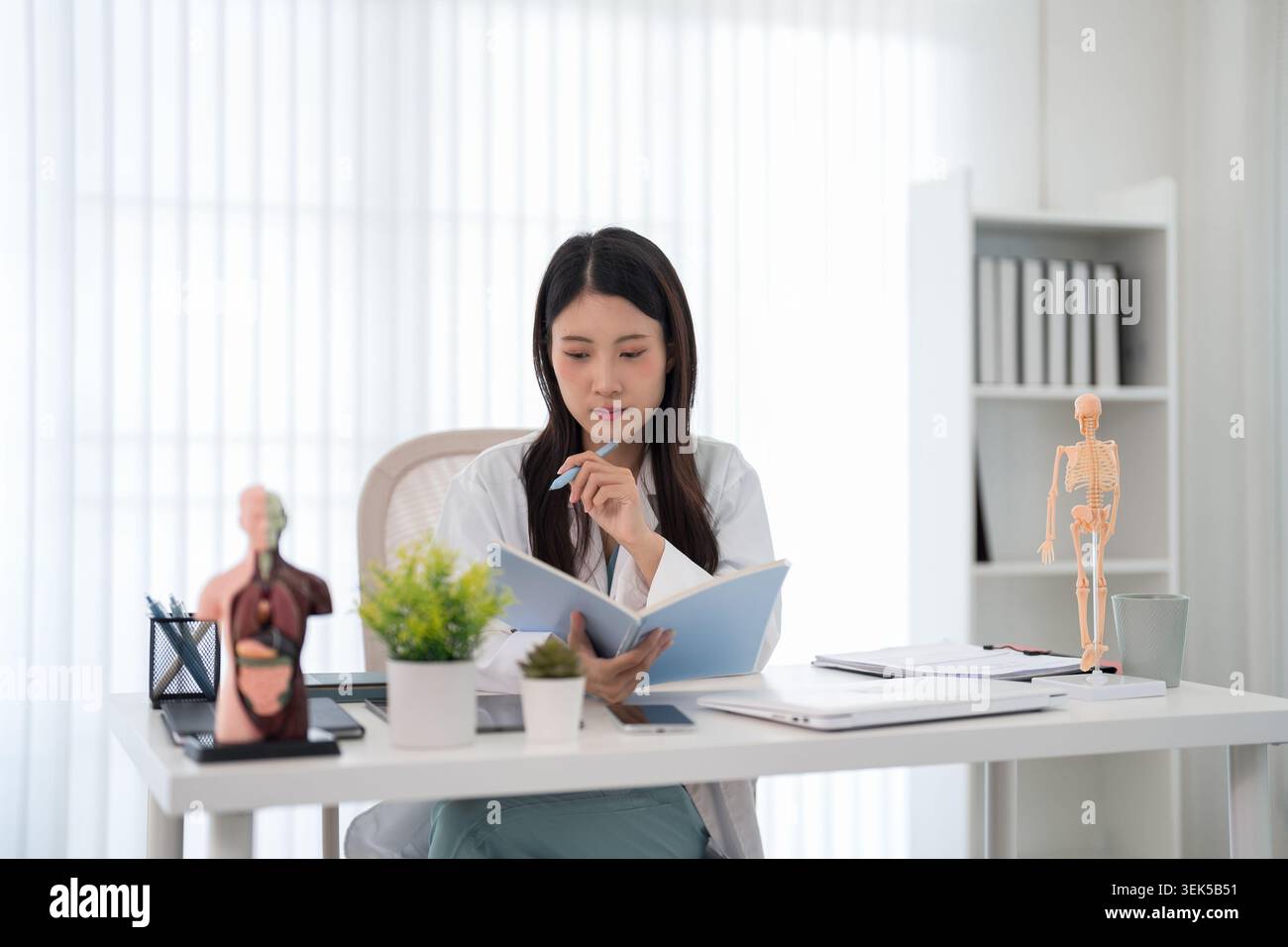 Young Asian female medical professional reading textbook at desk with ...