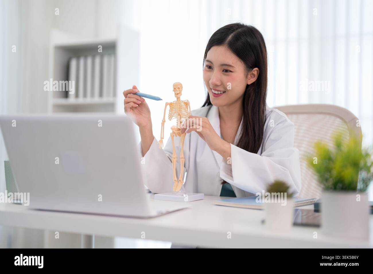 Asian adult woman doctor presenting human skeleton model during online ...
