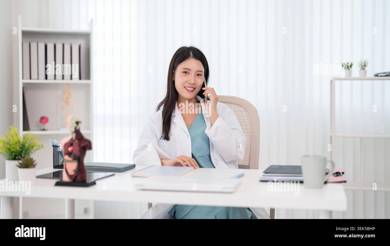 Young Asian female doctor speaking on smartphone at modern office desk ...
