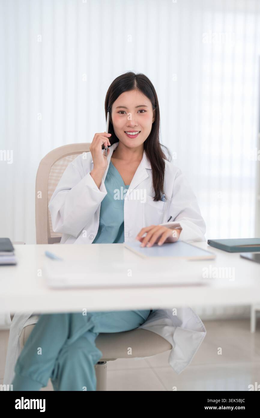 Asian doctor woman wearing white medical coat talking on phone smiling ...