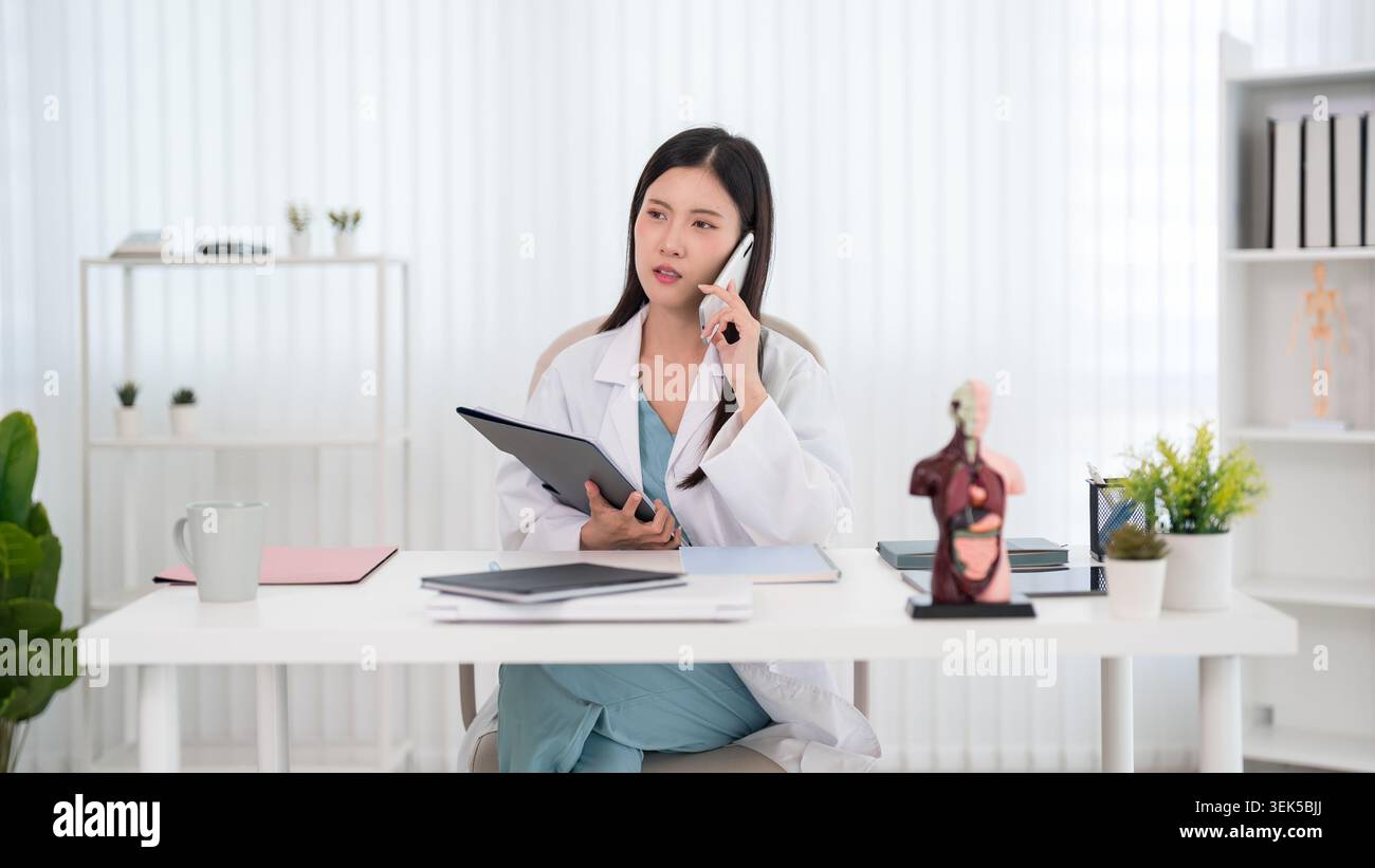 Asian female doctor talk phone call consult patient holding clipboard ...