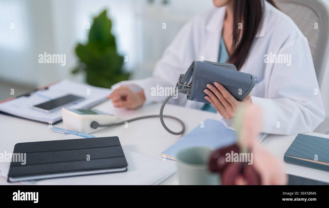 Female doctor using blood pressure monitor measurement device at clinic ...