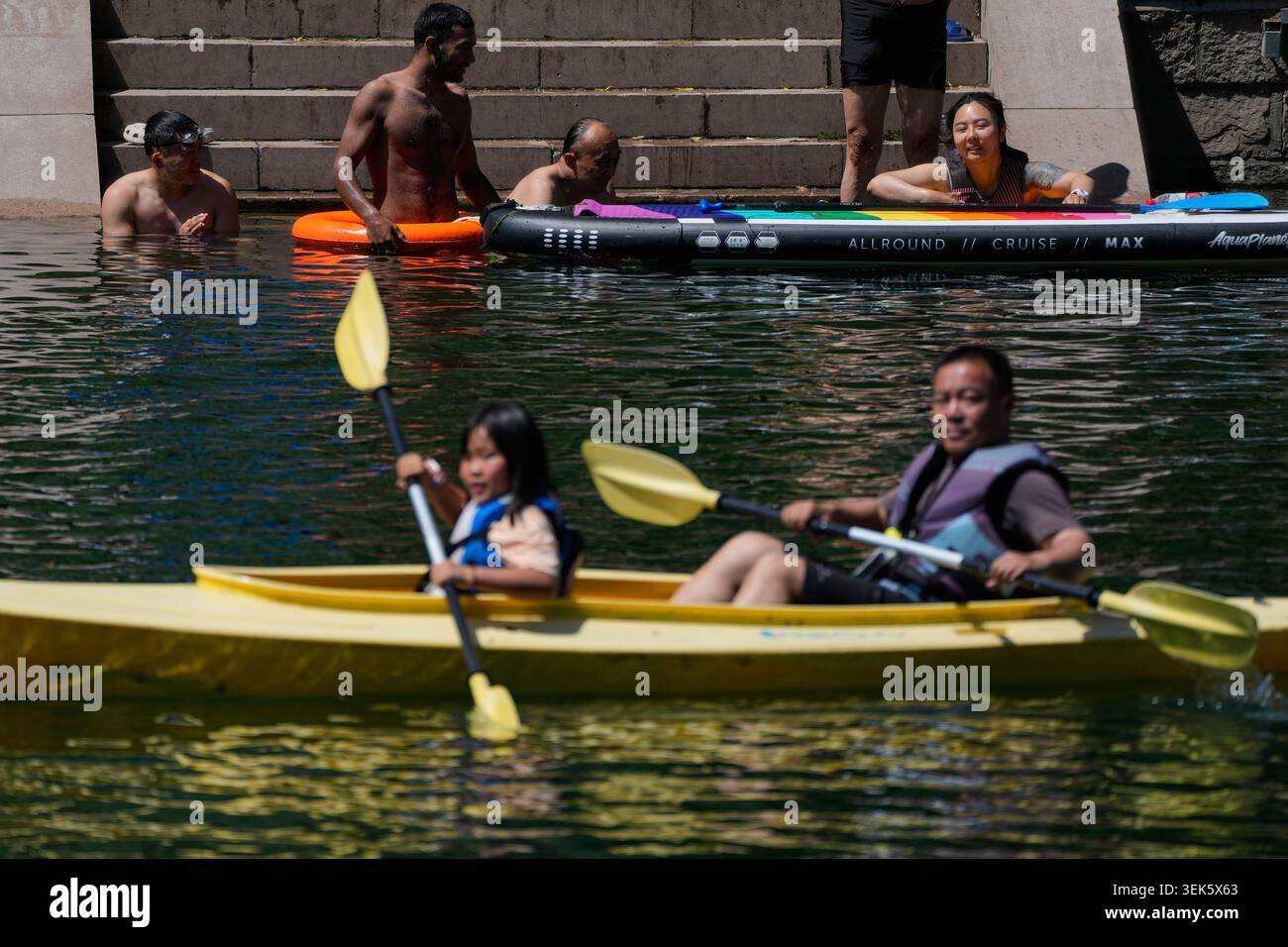 A man and a child kayak past as residents cool themselves at the ...