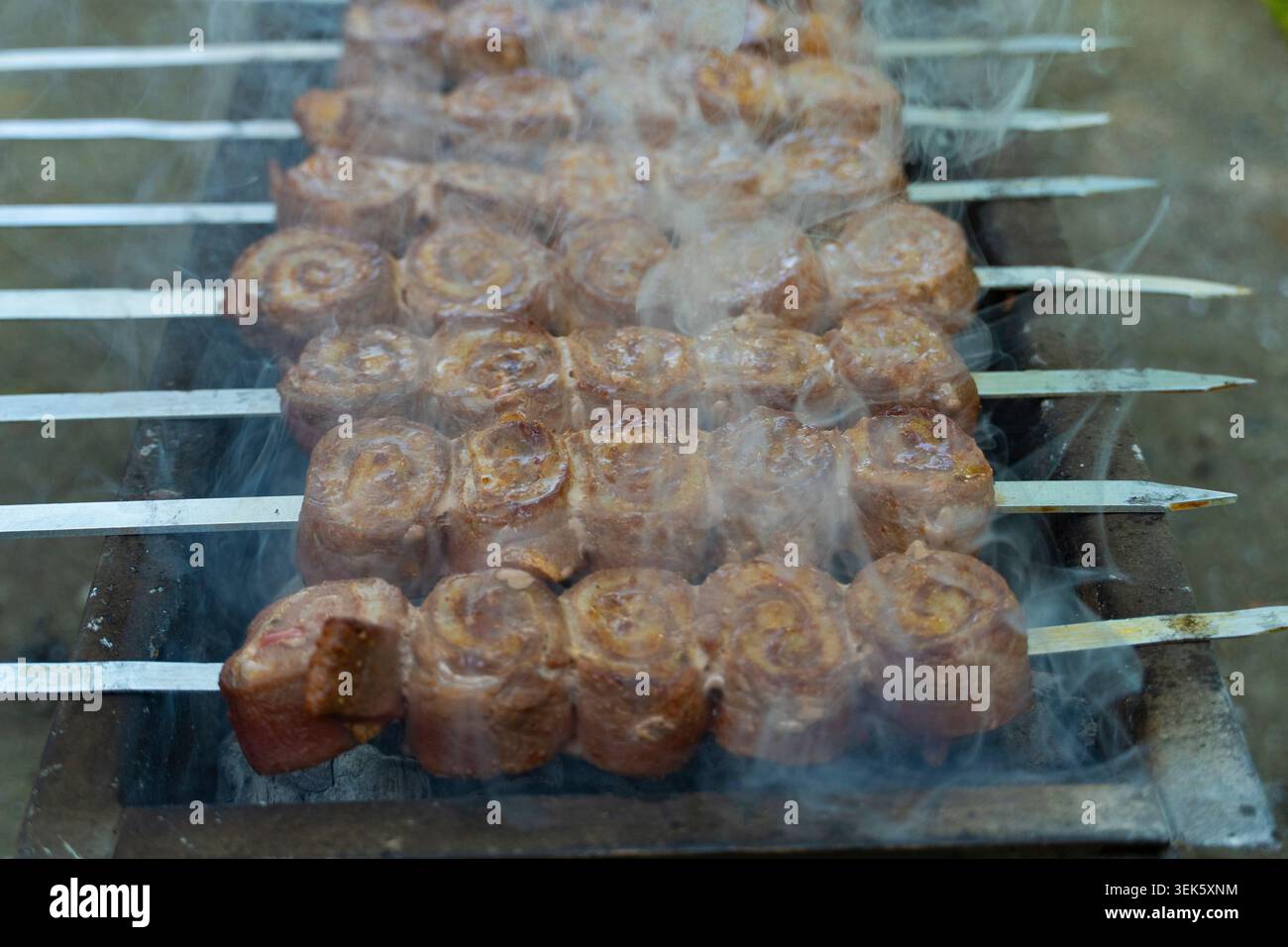 Juicy meat rolls cooking on metal skewers over hot charcoal with ...