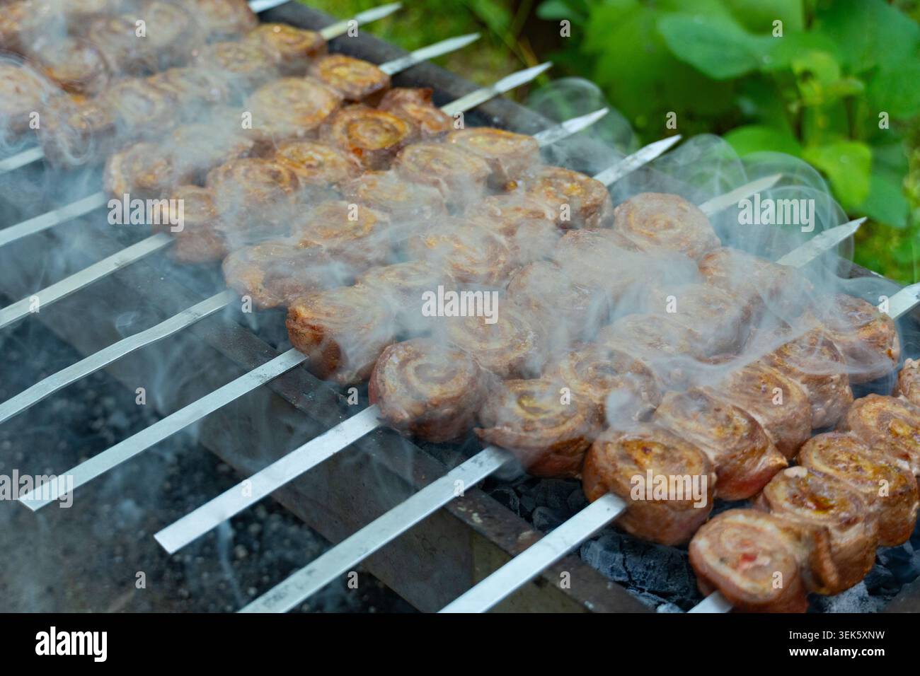 Juicy meat rolls cooking on metal skewers over hot charcoal with ...