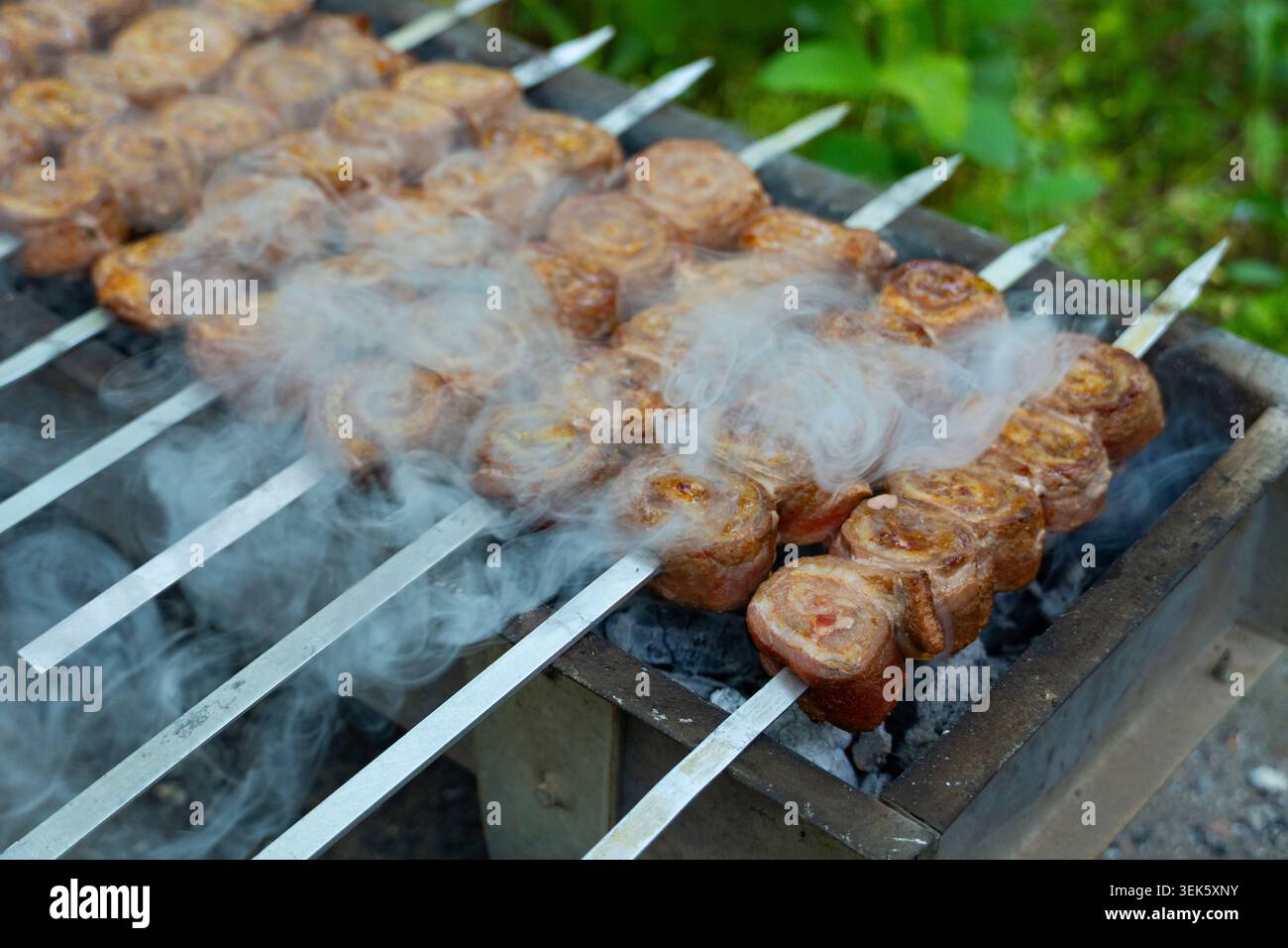 Juicy meat rolls cooking on metal skewers over hot charcoal with ...