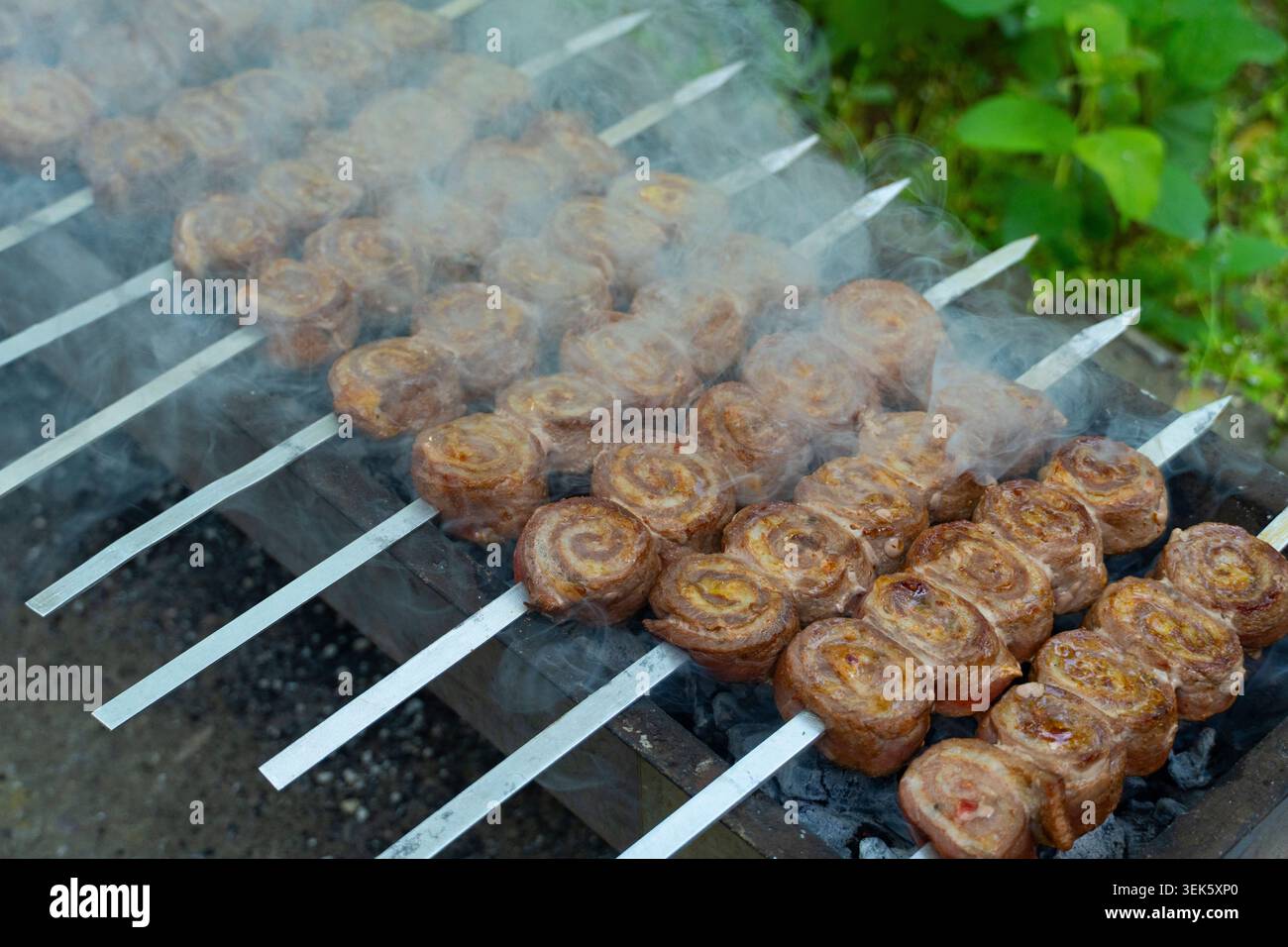 Juicy meat rolls cooking on metal skewers over hot charcoal with ...