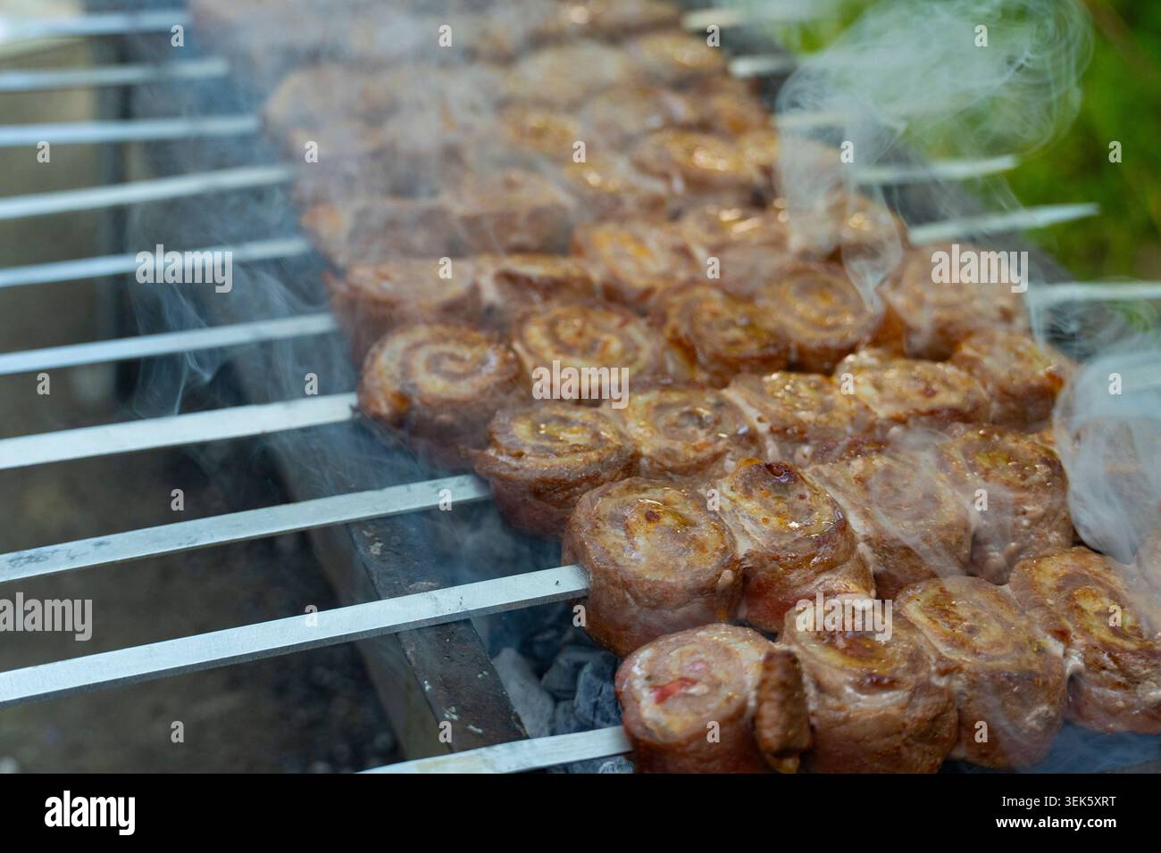 Juicy meat rolls cooking on metal skewers over hot charcoal with ...