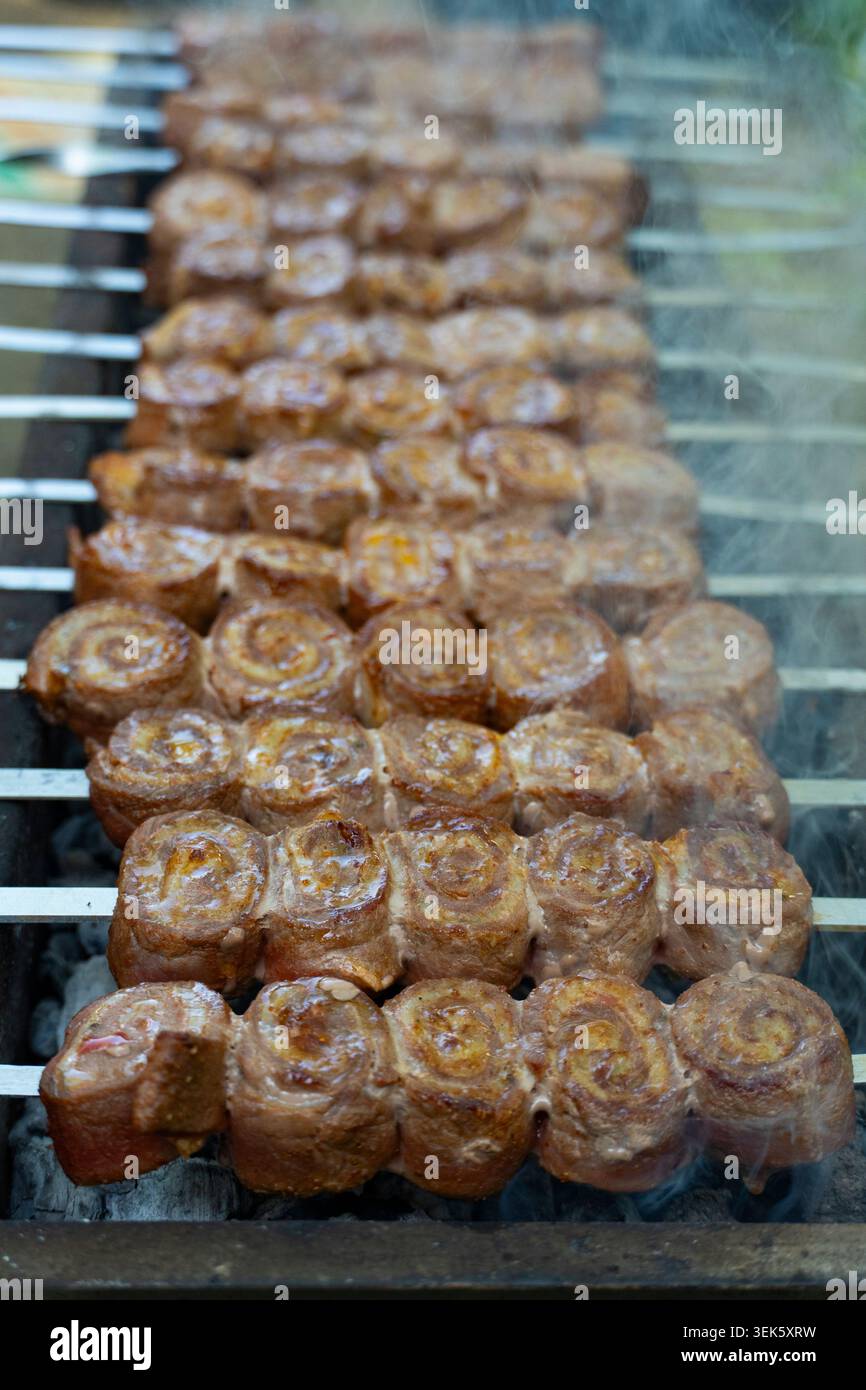 Juicy meat rolls cooking on metal skewers over hot charcoal with ...