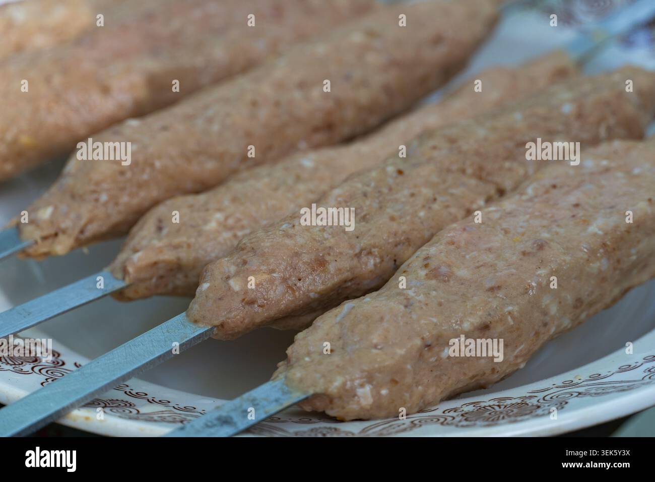 Close-up of raw minced meat kebabs shaped on flat skewers, placed on ...