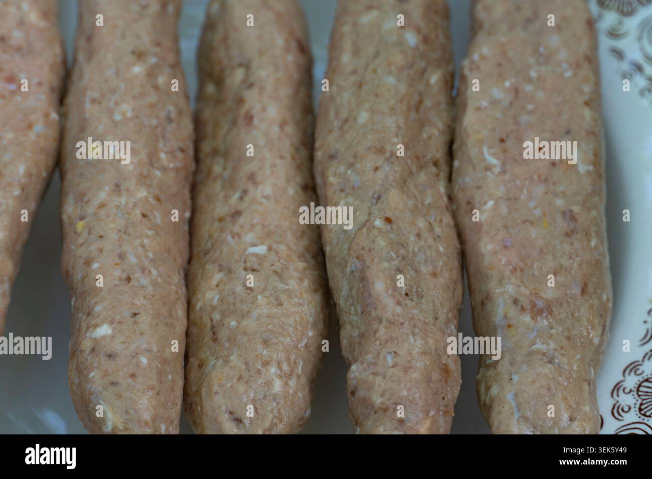 Close-up of raw minced meat kebabs shaped on flat skewers, placed on ...
